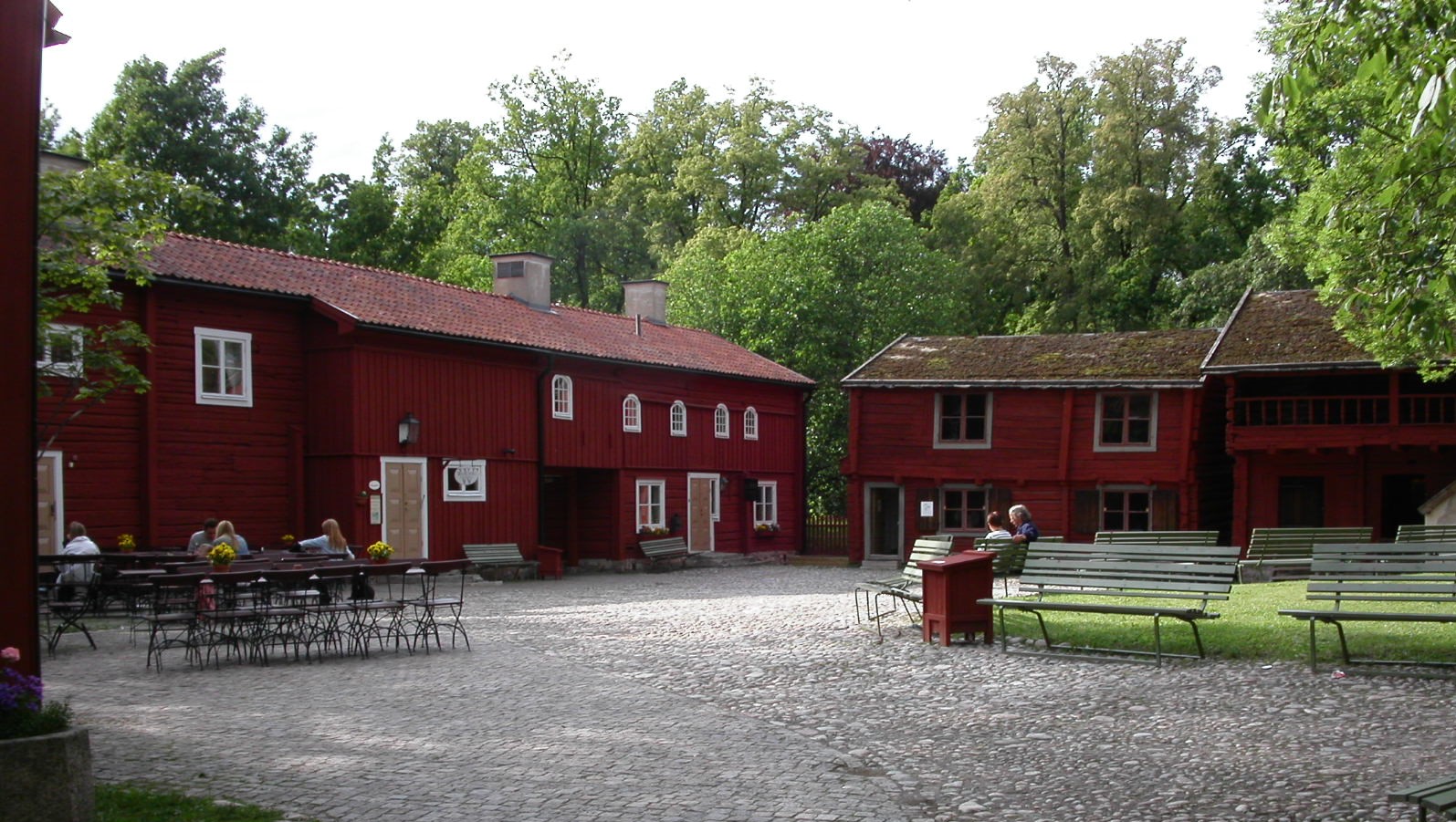 Röda gamla trähus vid ett torg av kullersten. På torget ses även ...